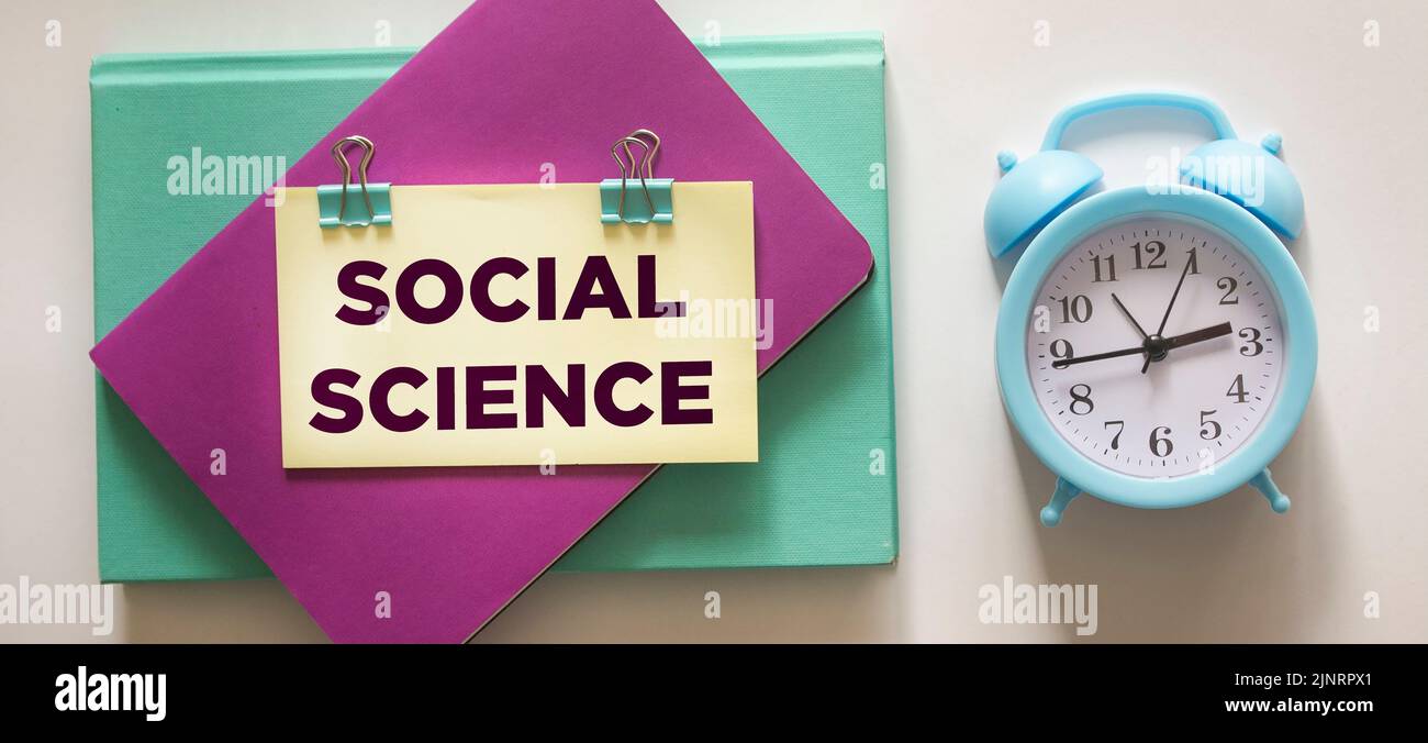 Social science memo written on a notepad, next to a clock on a white ...