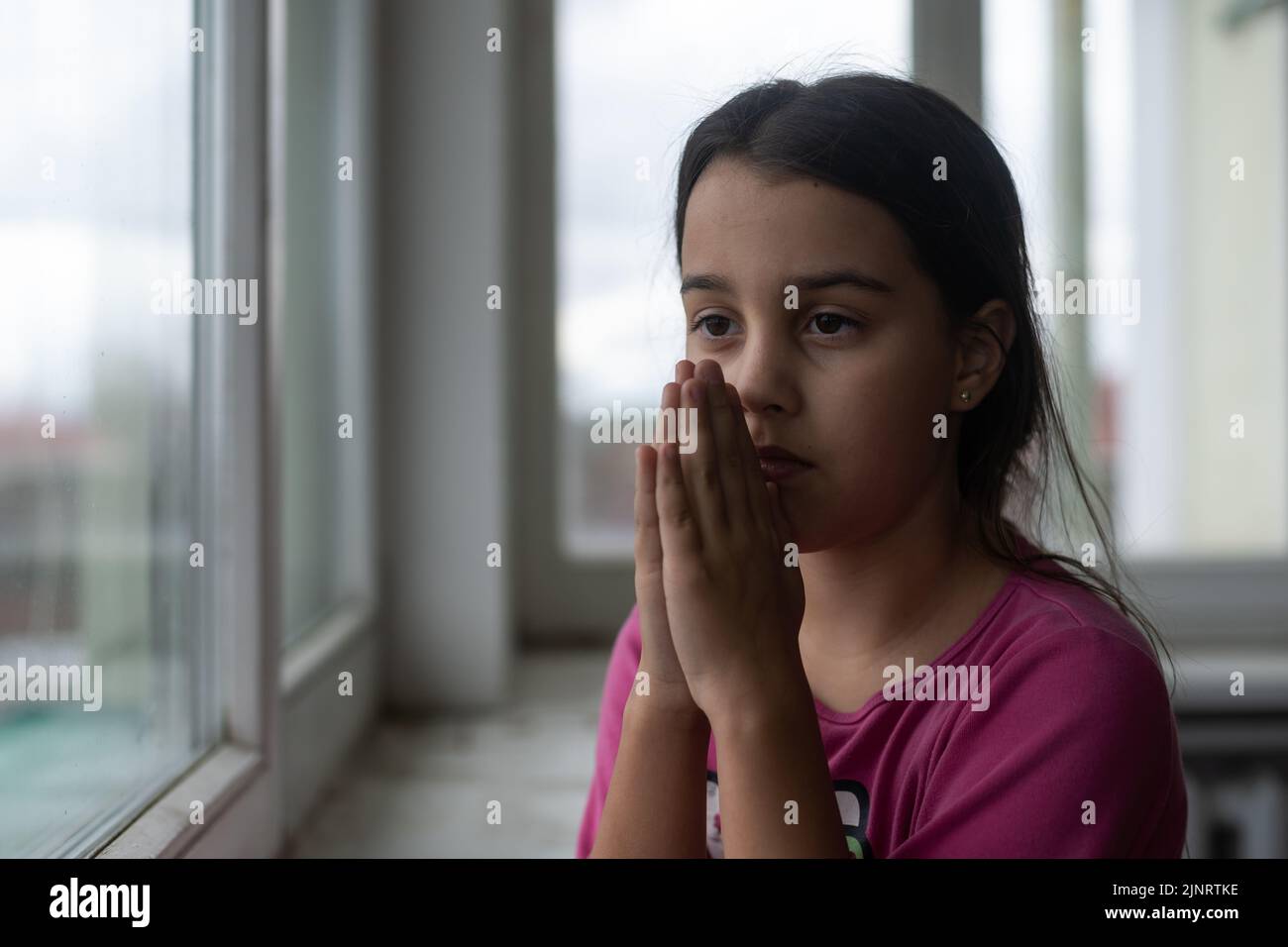 Praying little girl near window Stock Photo - Alamy
