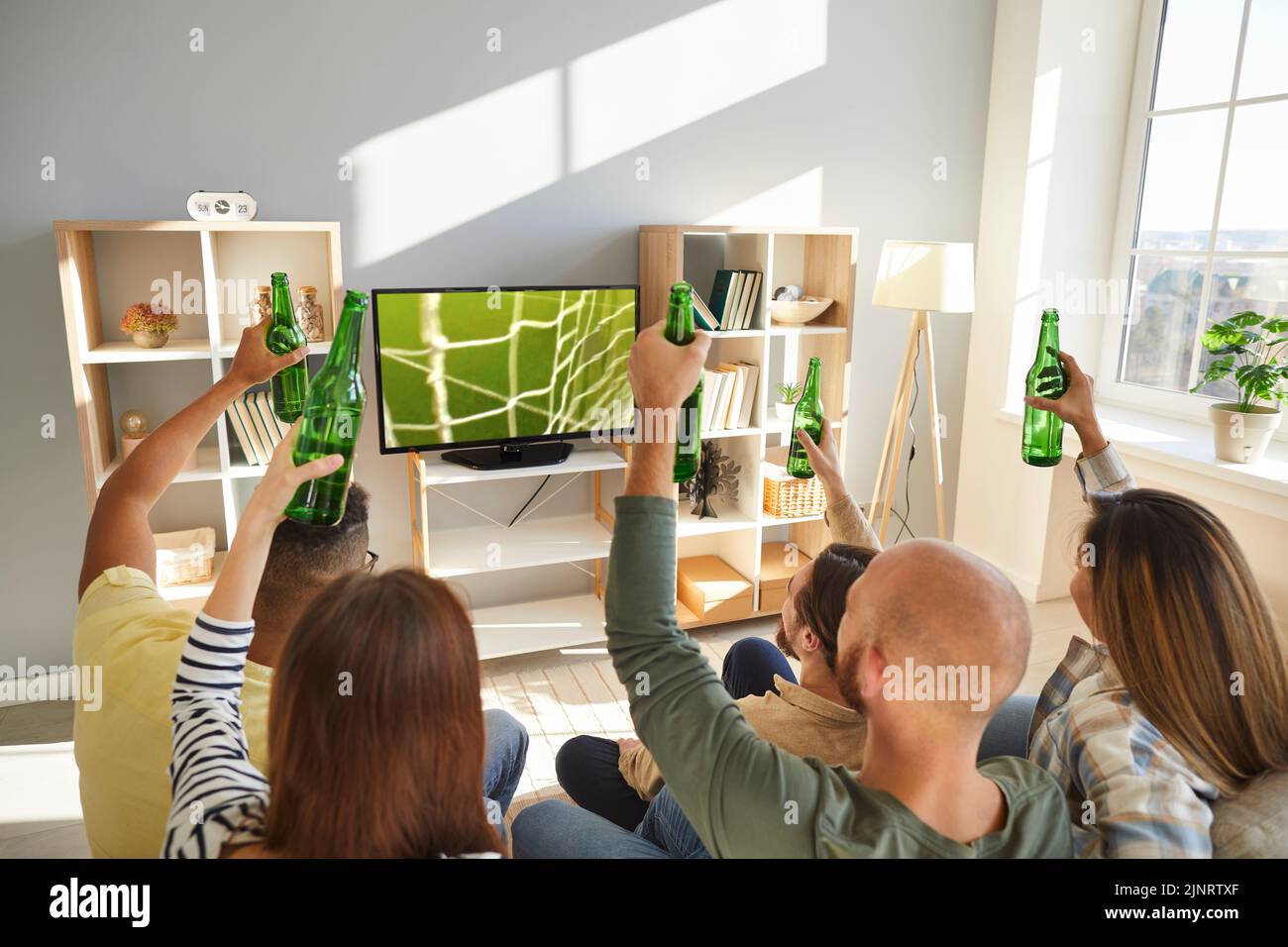 Happy young friends sitting on the couch, watching football on TV and ...