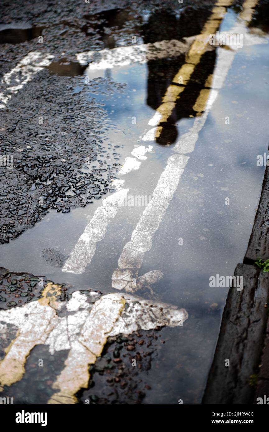 Puddle with clouds and building in reflection with the double yellow ...