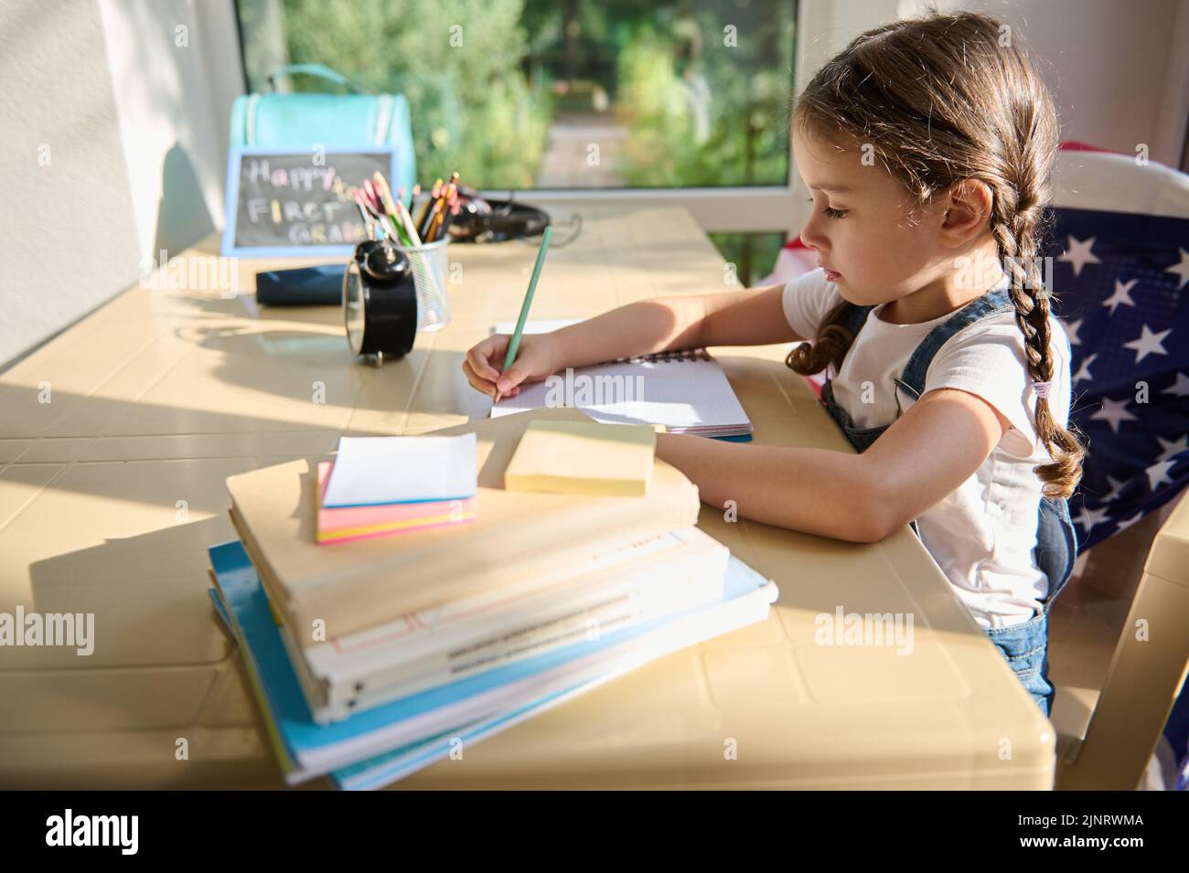Adorable school girl, primary student sitting at a table and is focused ...