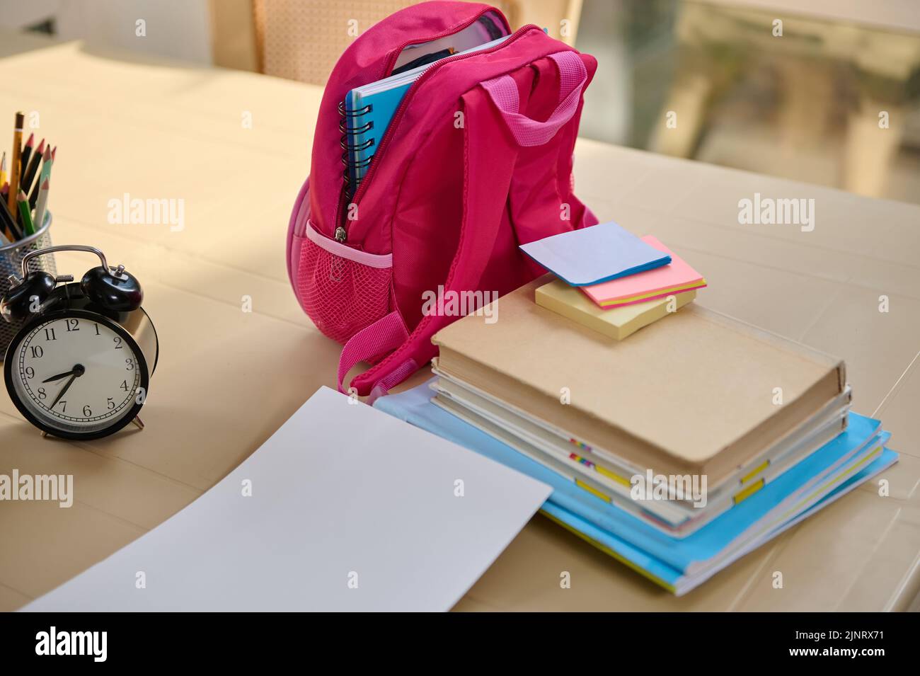 Pink backpack and stacked textbooks near a black alarm clock on the ... Pink backpack and stacked textbooks near a black alarm clock on the ...
