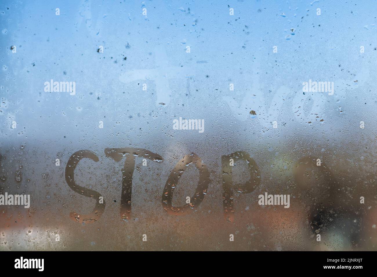 the word stop written on night wet window glass close-up with blurred ...