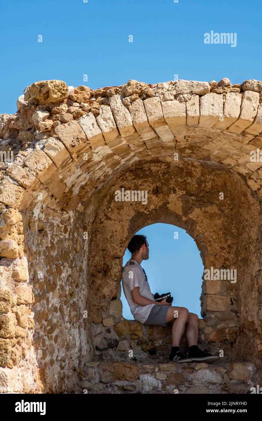 young man sitting in an arched window in the ruins of the coastal ...