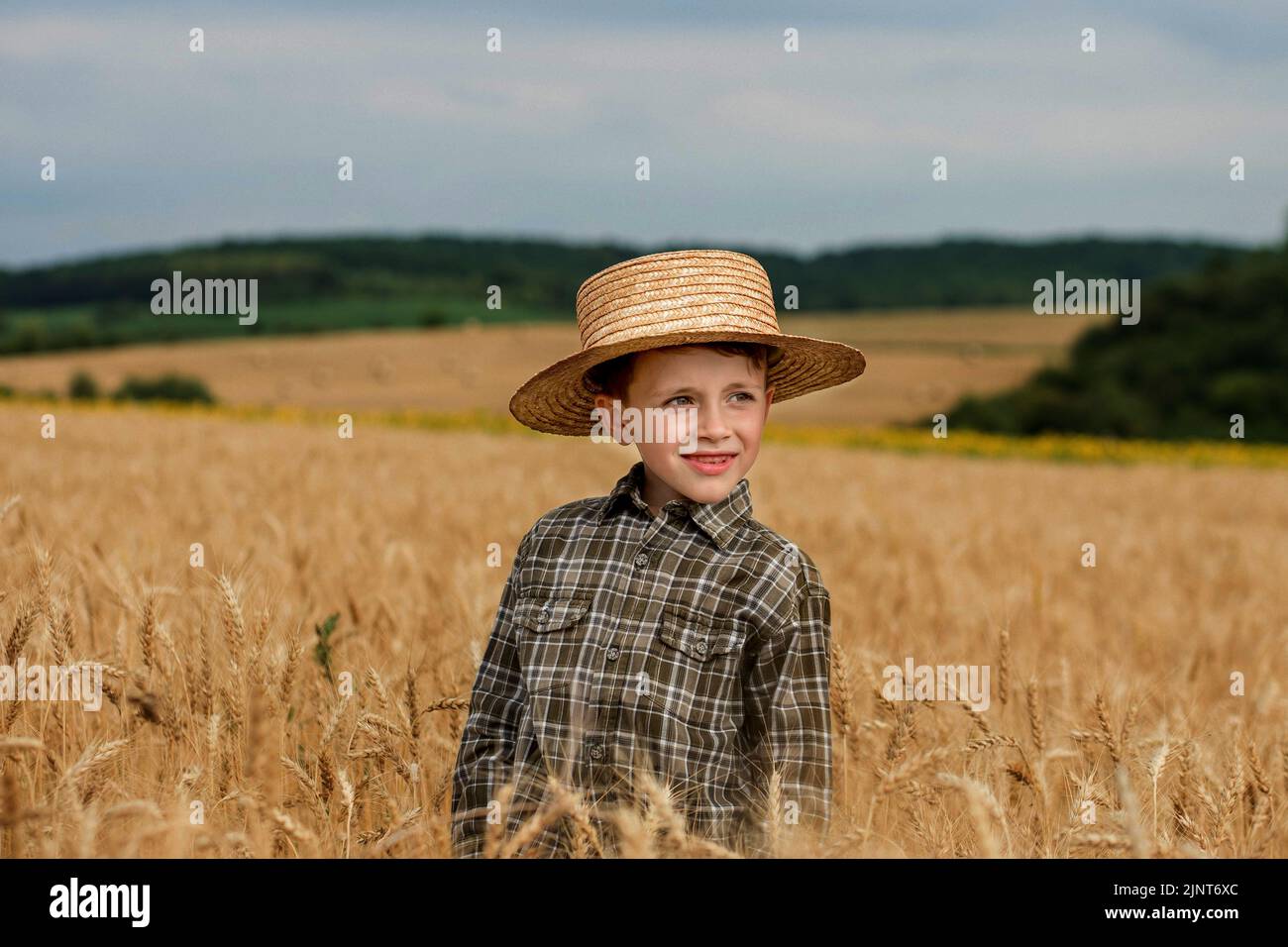 A smiling little farmer boy in a plaid shirt and straw hat poses for a ...