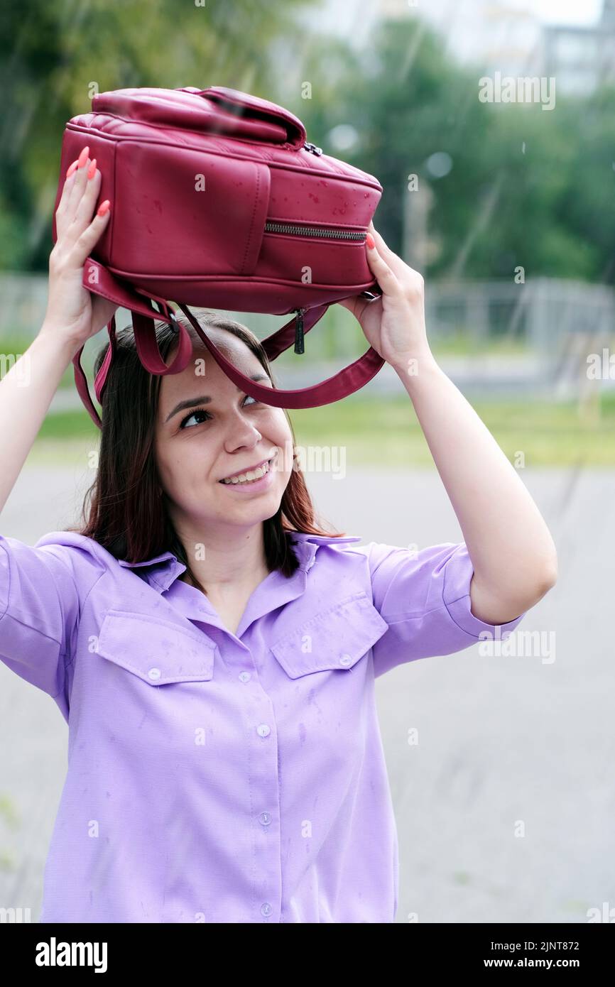 Young woman on street in rain. Positive female in purple shirt holding ...