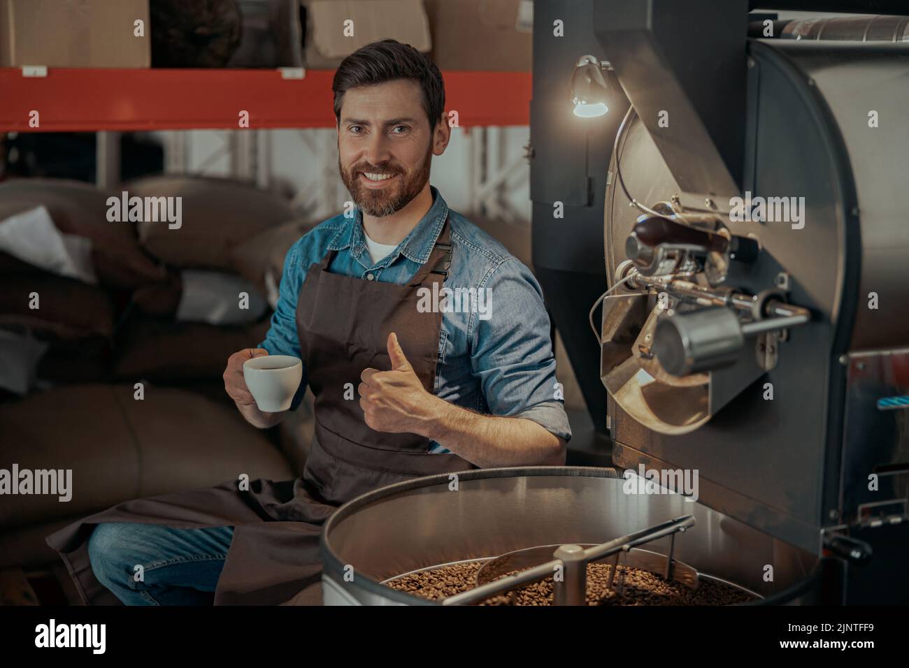 Barista drinking coffee sitting near coffee roasting machine with rise ...