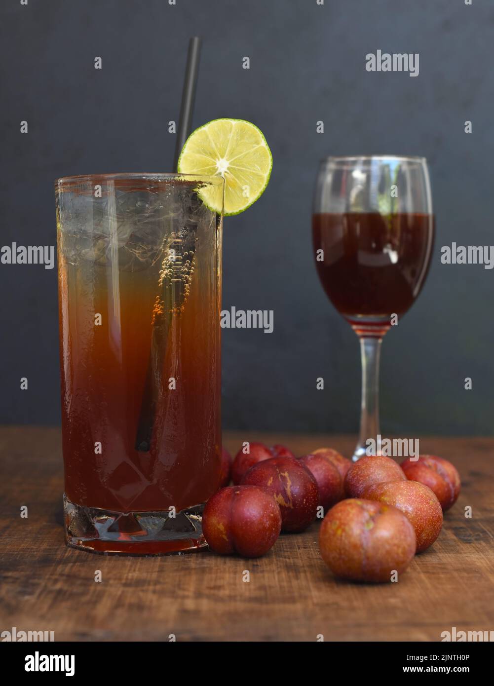 Plum wine highball cocktail with glass of wine and plums on wooden table and black background ...