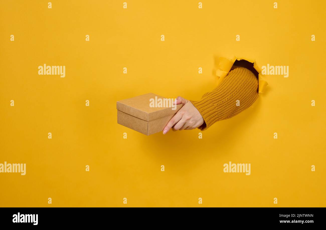 A woman's hand holds a brown cardboard box, part of the body sticks out ...
