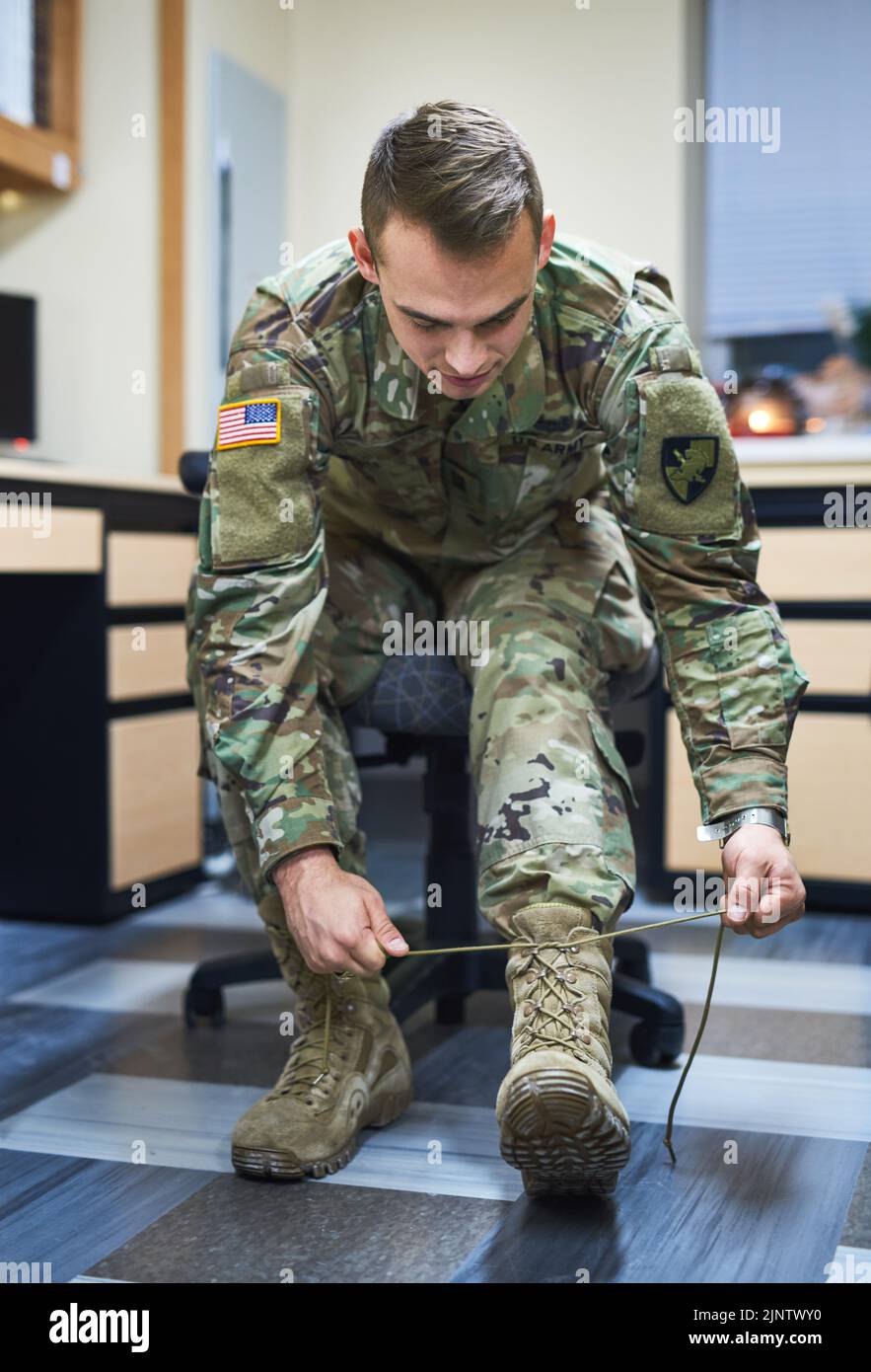Battle is better in boots. a young soldier tying his boot shoelaces in ...