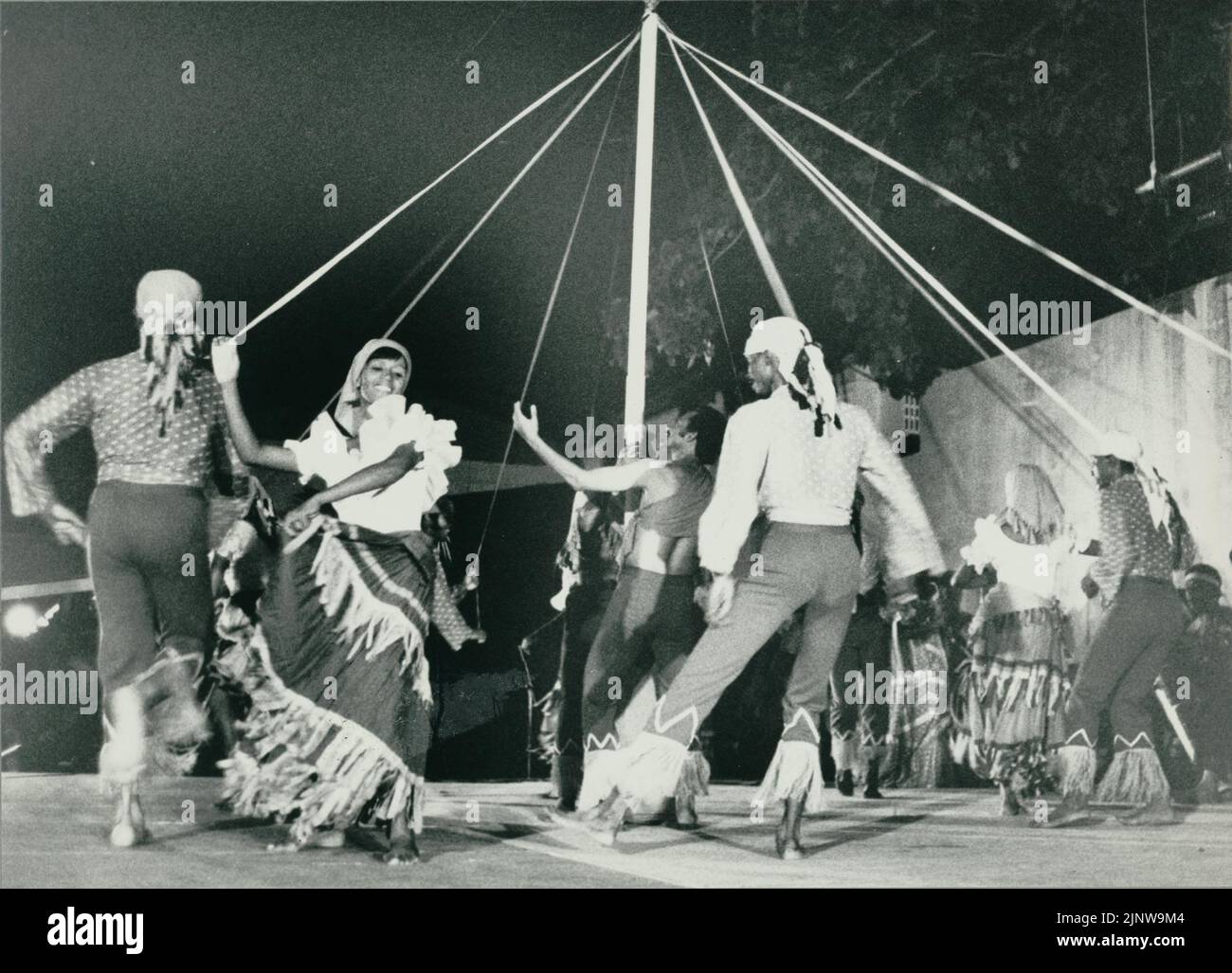 Black and white photograph of people wearing costumes dancing around a ...
