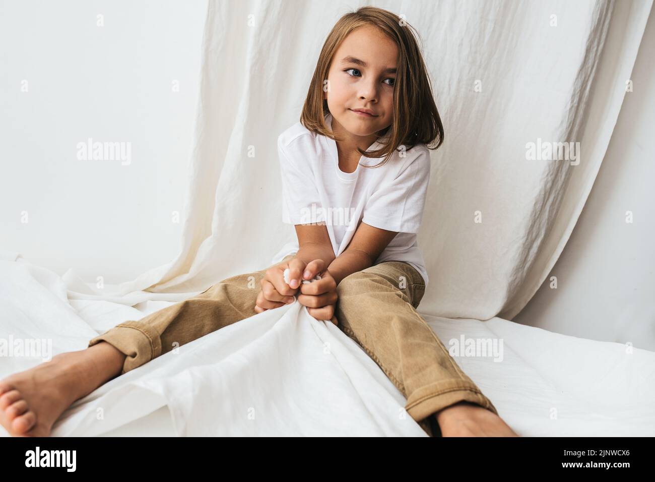 Thoughtful insecure tween girl sitting on a table cramping a white ...