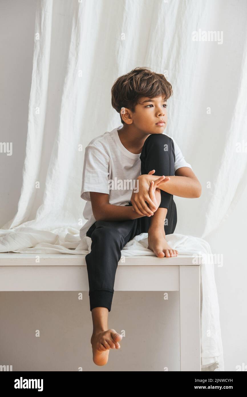 Thoughtful bored and sad indian boy sitting on a table, looking nowhere ...