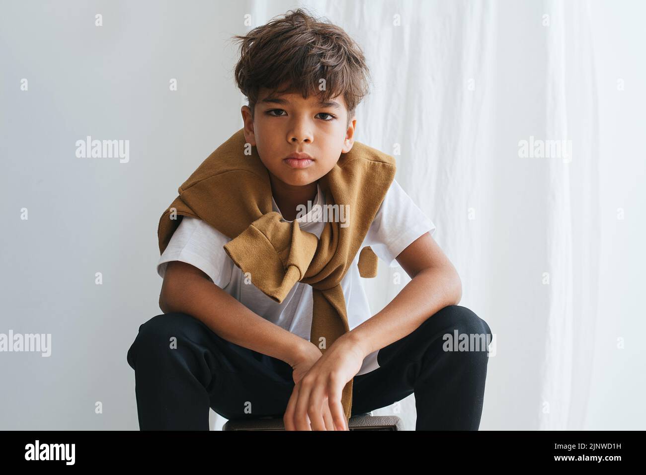 Slouching indian boy sitting on a low pedestal, looking at the camera ...
