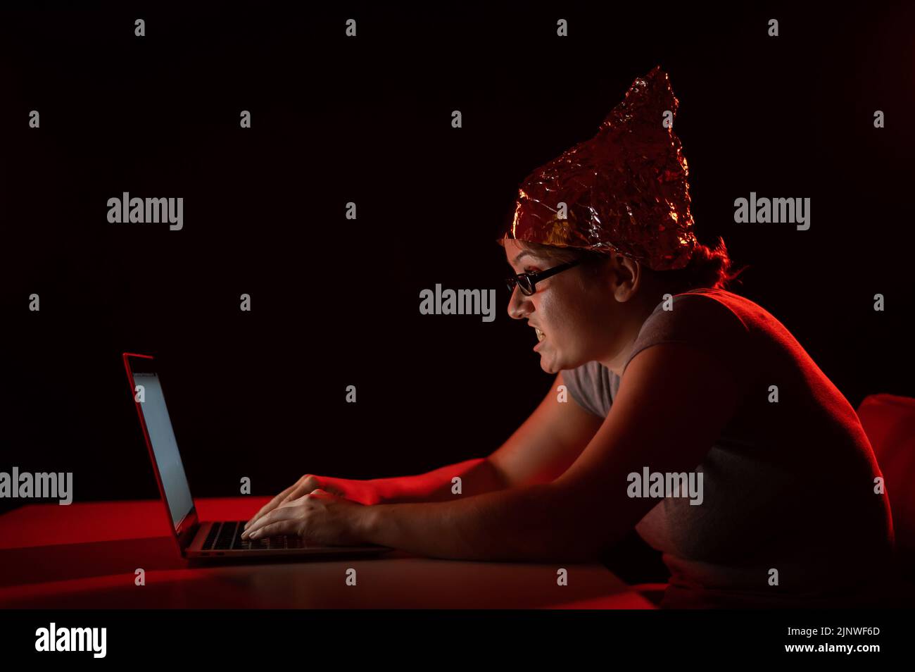 Paranoid caucasian woman typing on a computer wearing a tinfoil cap ...