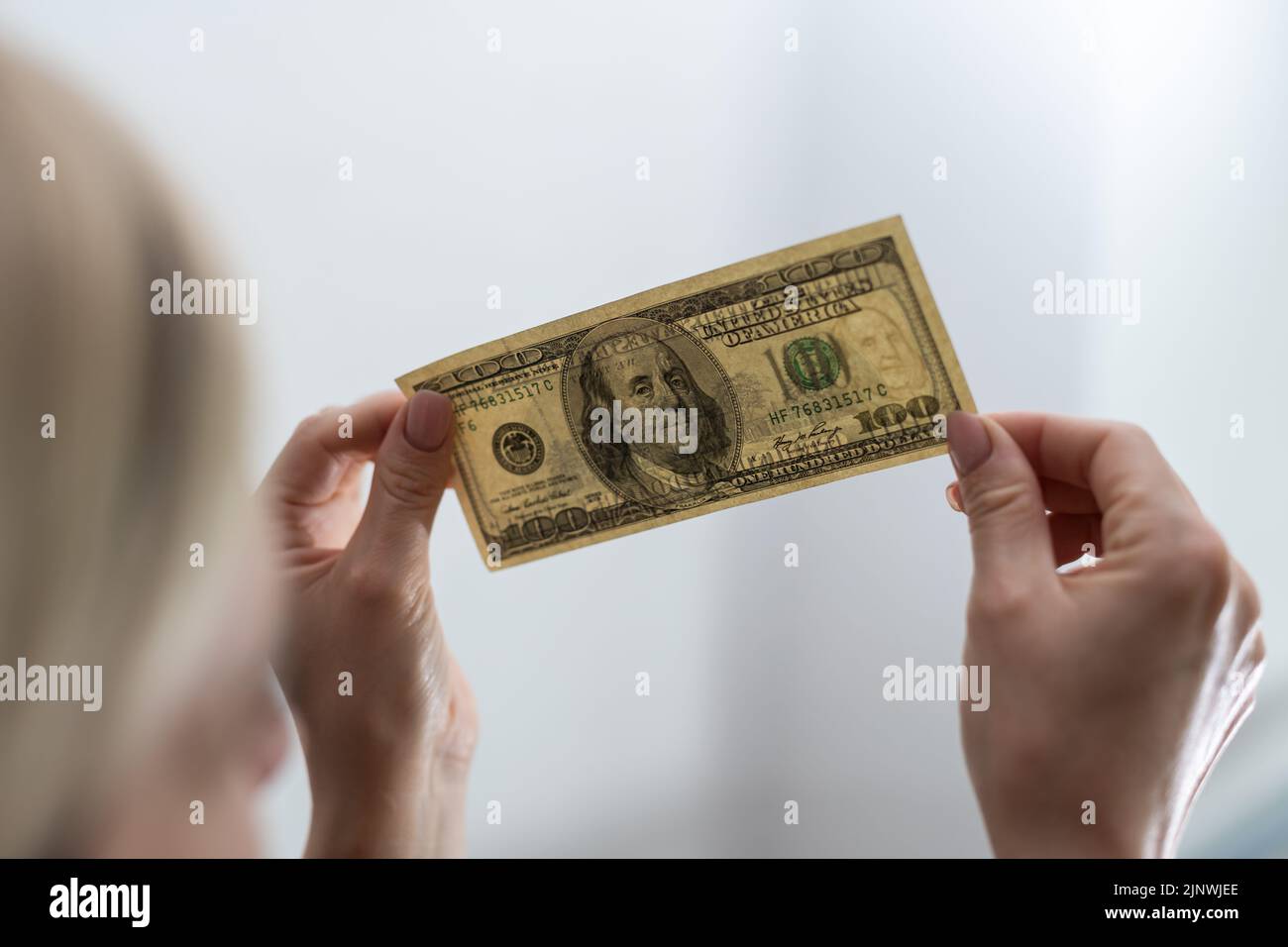 Checking counterfeit money light. 100 dollars against the window in his ...