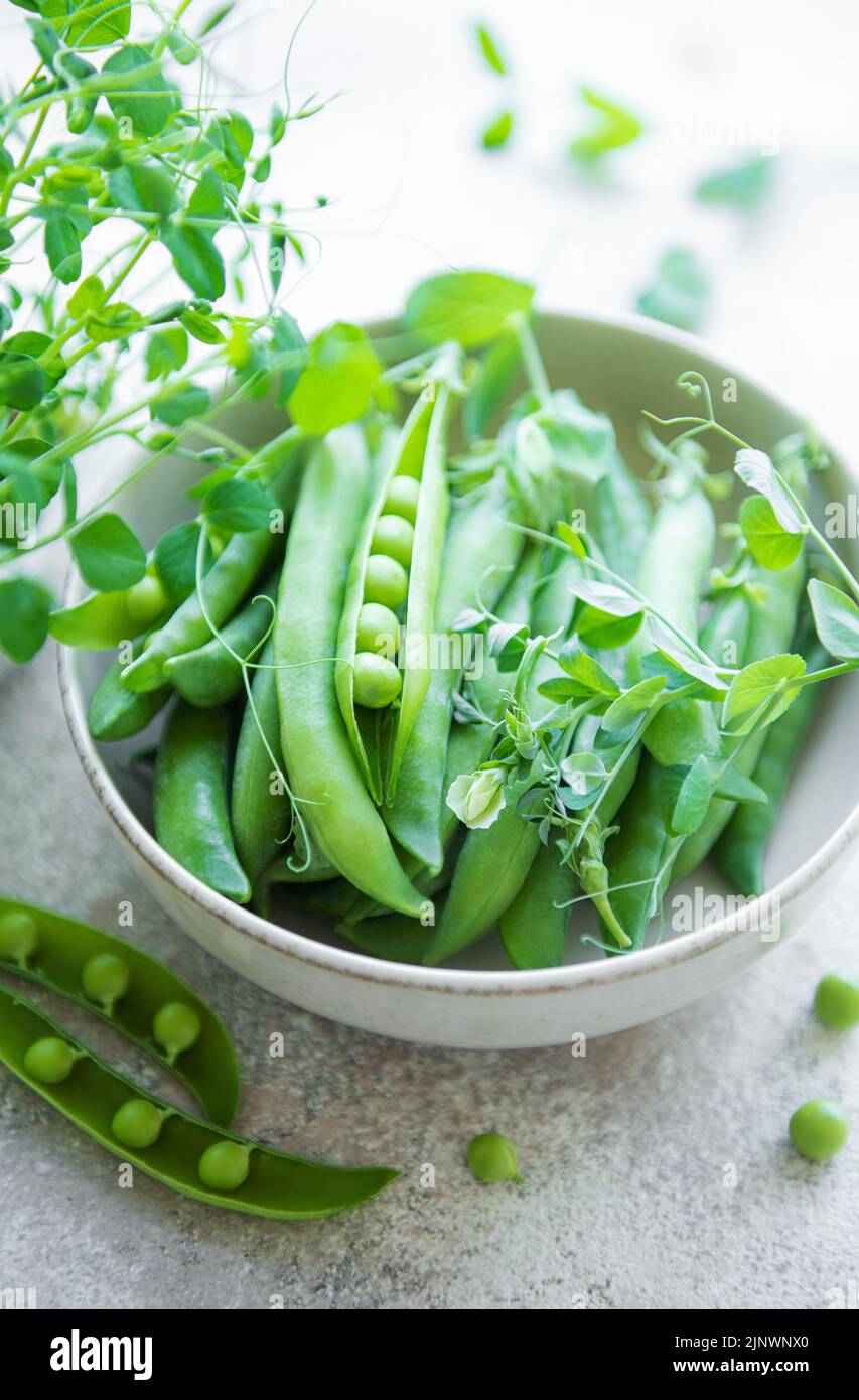 Bowl with young fresh juicy pods of green peas on a concrete background ...