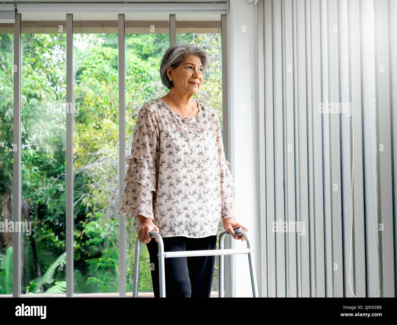 Asian senior woman, white hair standing with walking frame and looking ...