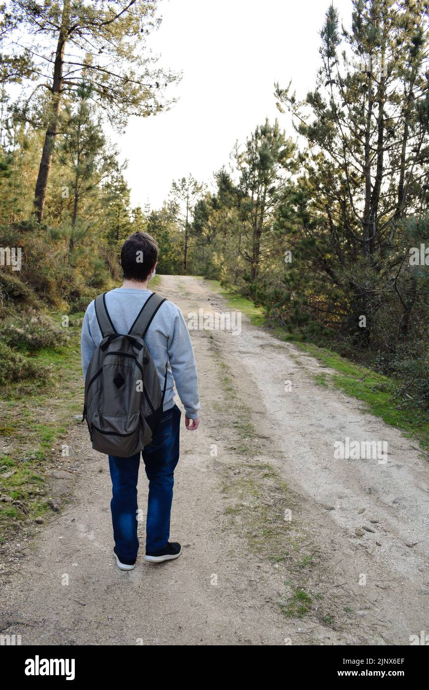Back view of a teenager with a backpack walking on a path through the ...