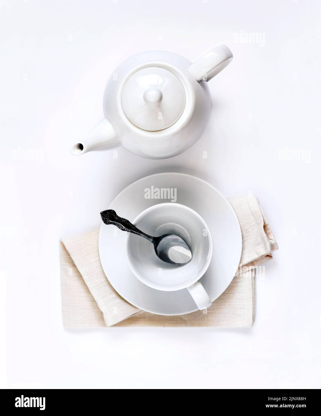 White teapot and empty teacup with spoon on pale beige cloth isolated ...