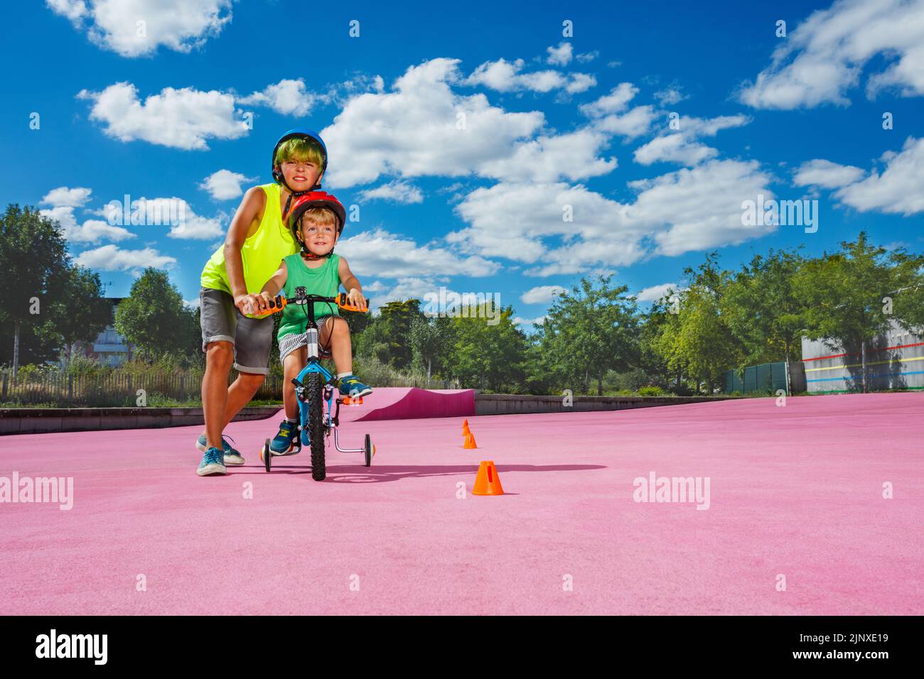 Boy help brother learn ride a bicycle going around orange cones Stock ...