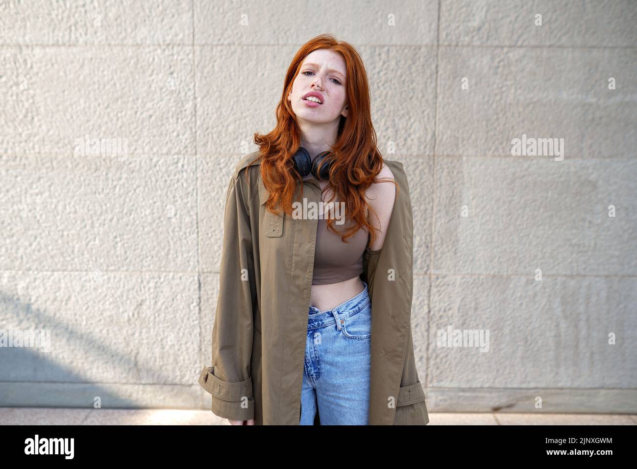 Redhead hipster girl standing on urban wall background looking bored ...