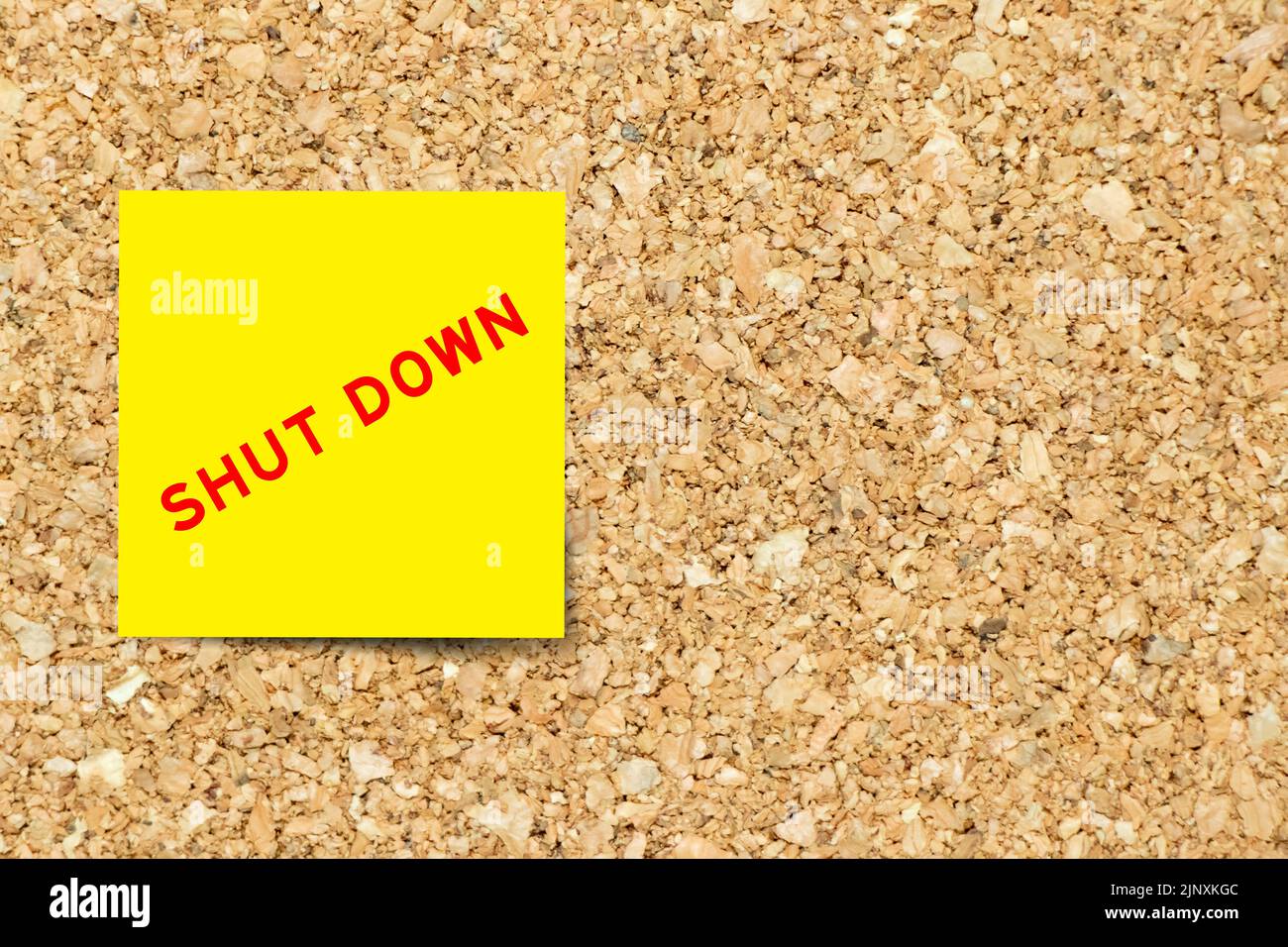 Yellow note paper with word shut down on cork board background with ...