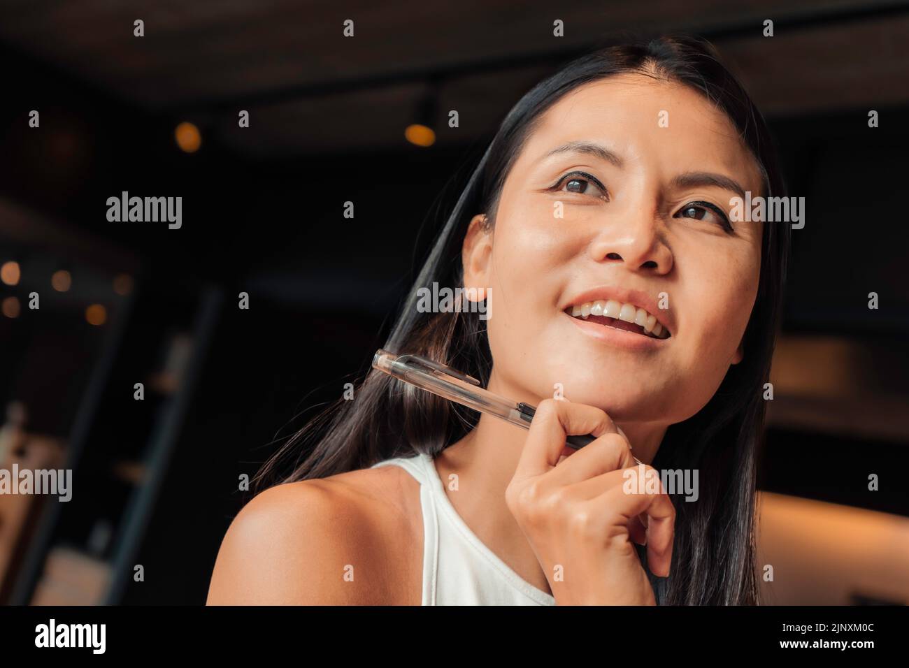 Smiling beautiful asian woman thinking and holding a pen Stock Photo ...