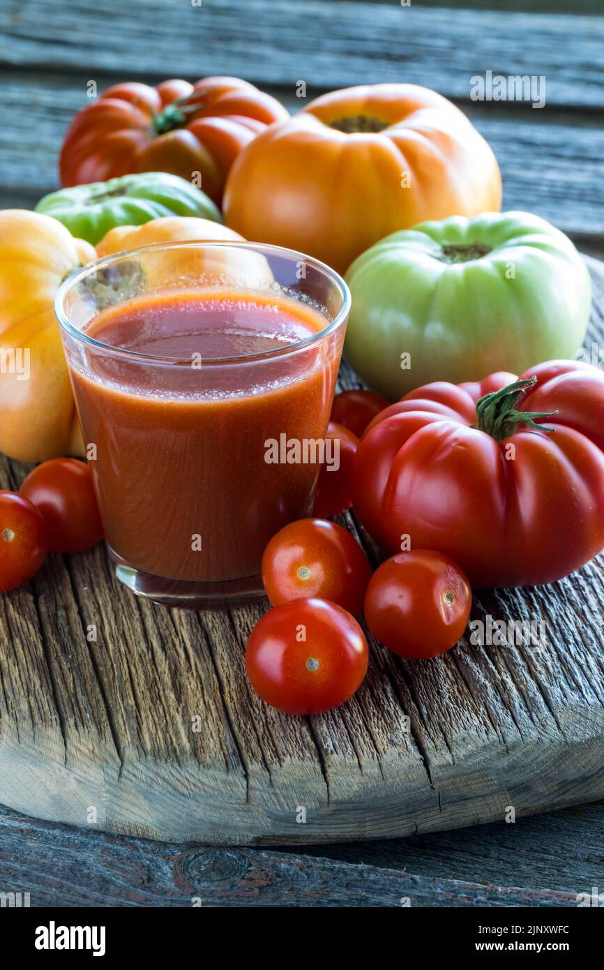 A glass of fresh tomato juice on a rustic board surrounded by various ...