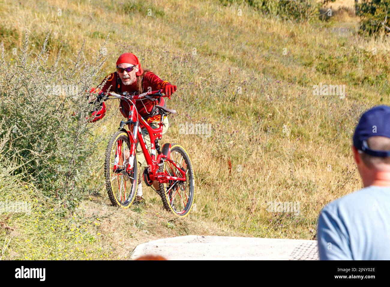 man dressed in red pushing red mountain bike up steep path countryside ...
