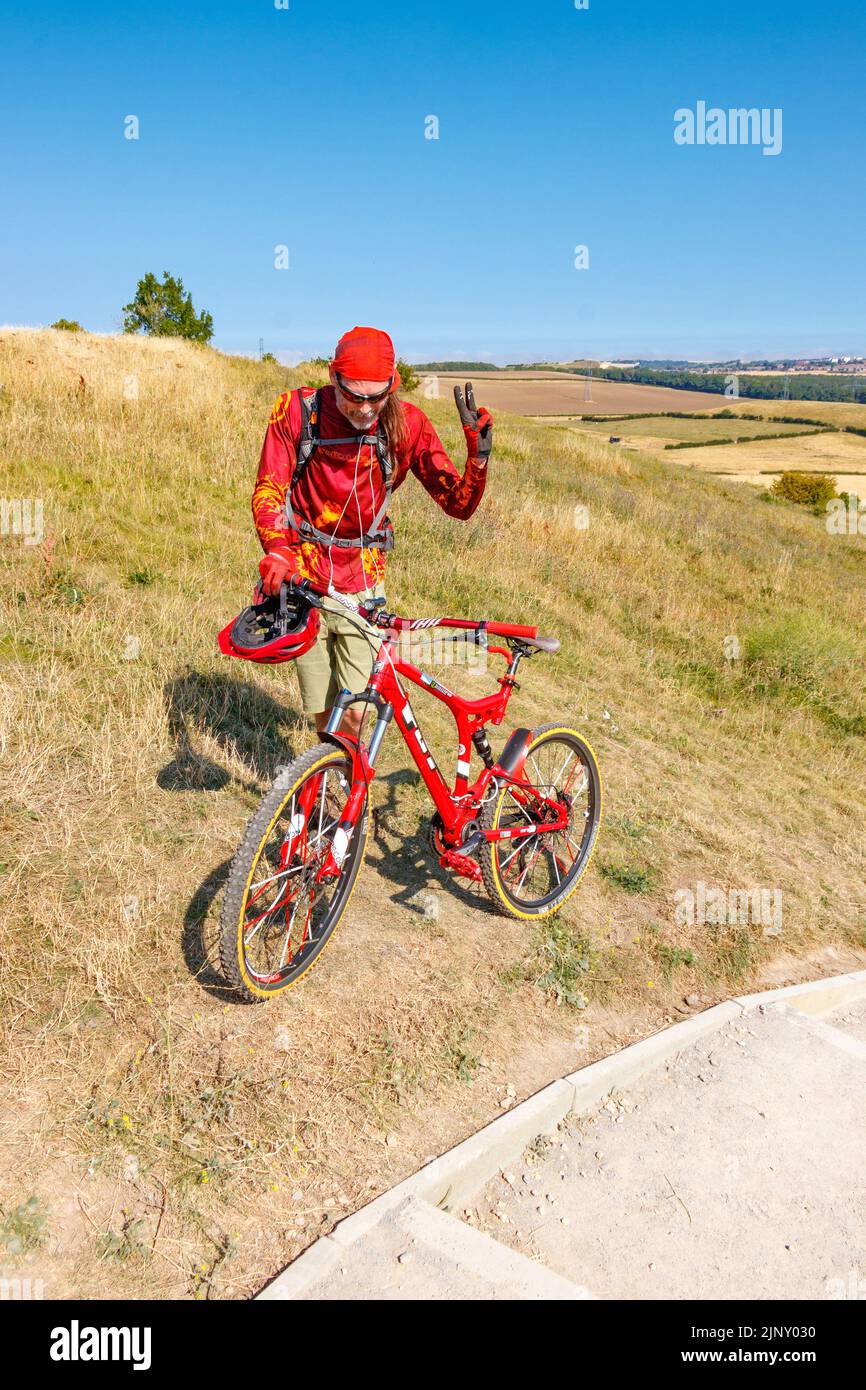 man dressed in red gives v sign mountain bike up steep path countryside ...