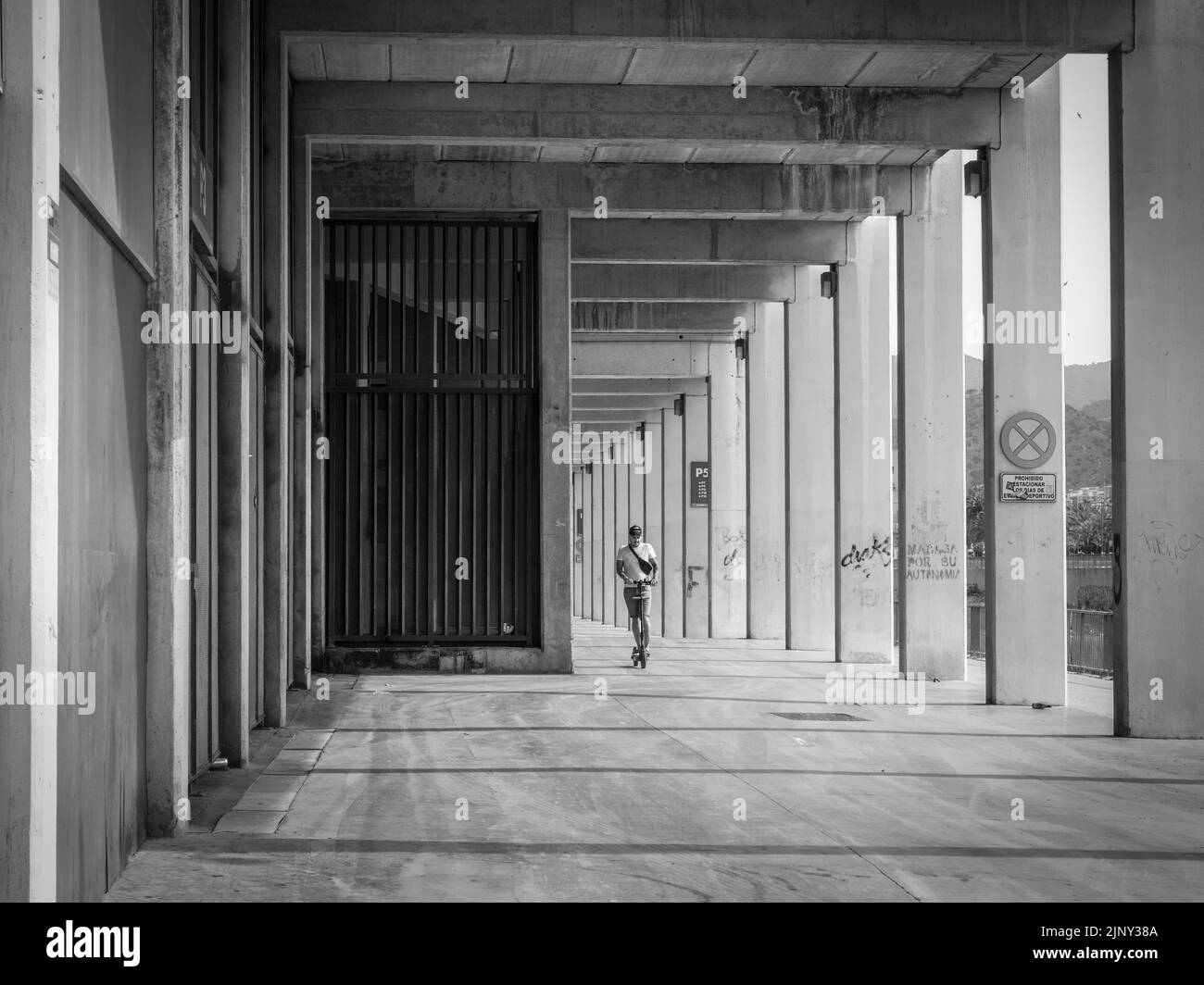 A young man on a scooter riding under a concrete column structure Stock ...