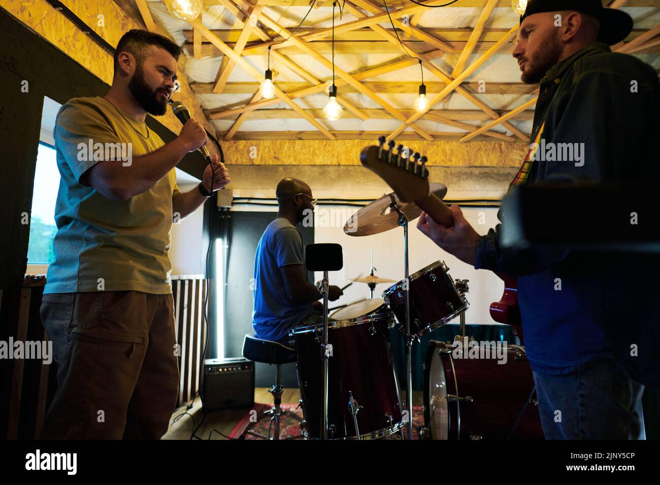 Bearded man singing in microphone among his buddies playing electric ...
