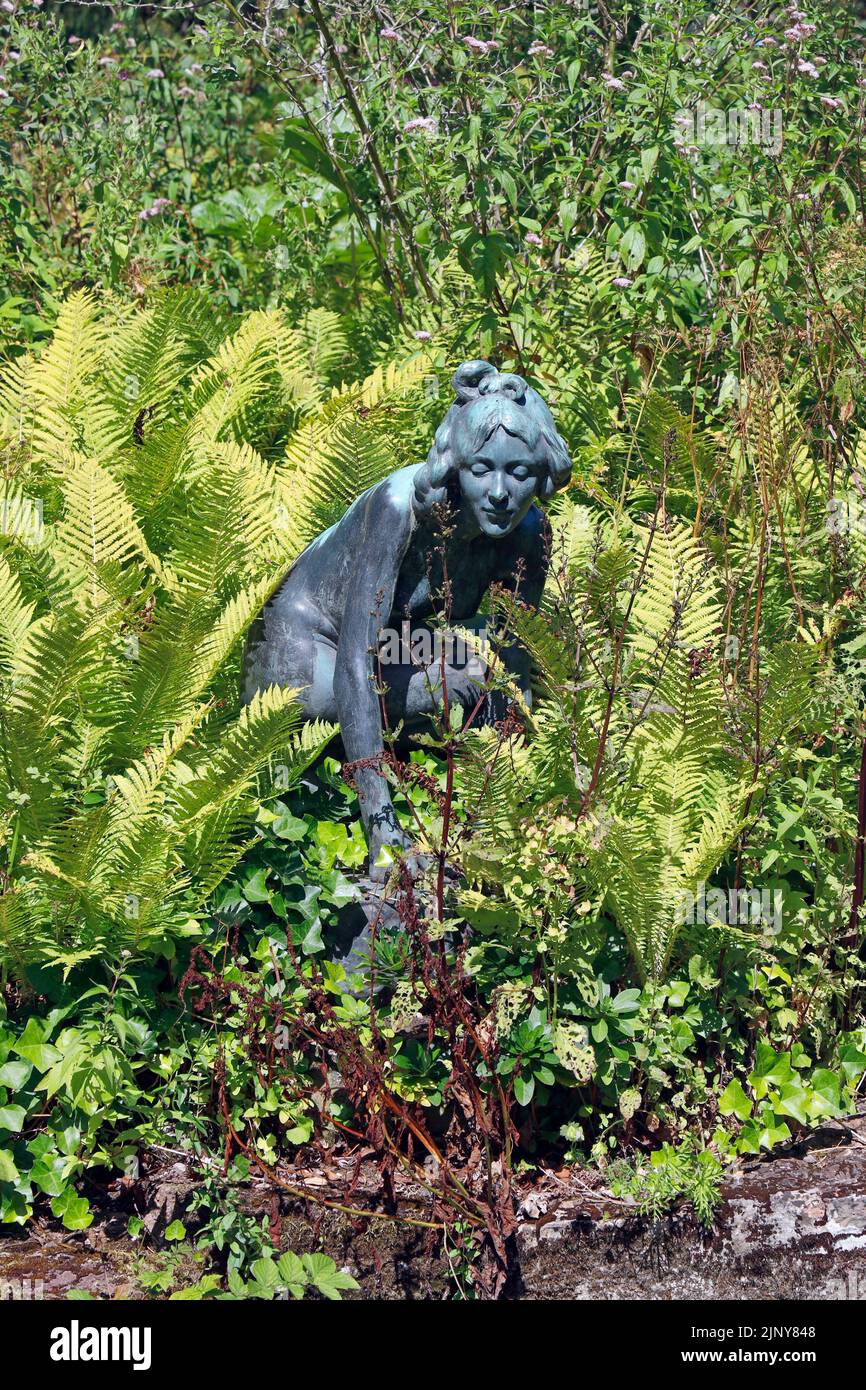 Water nymph statue, looking at reflecion in ornamental pond. Amongst ...