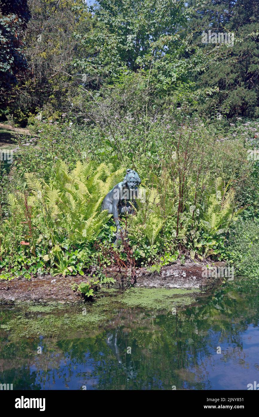 Water nymph statue, looking at reflecion in ornamental pond. Amongst ...