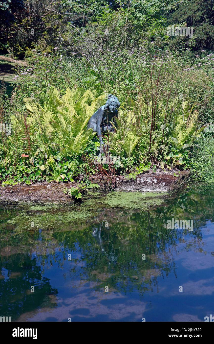 Water nymph statue, looking at reflecion in ornamental pond. Amongst ...