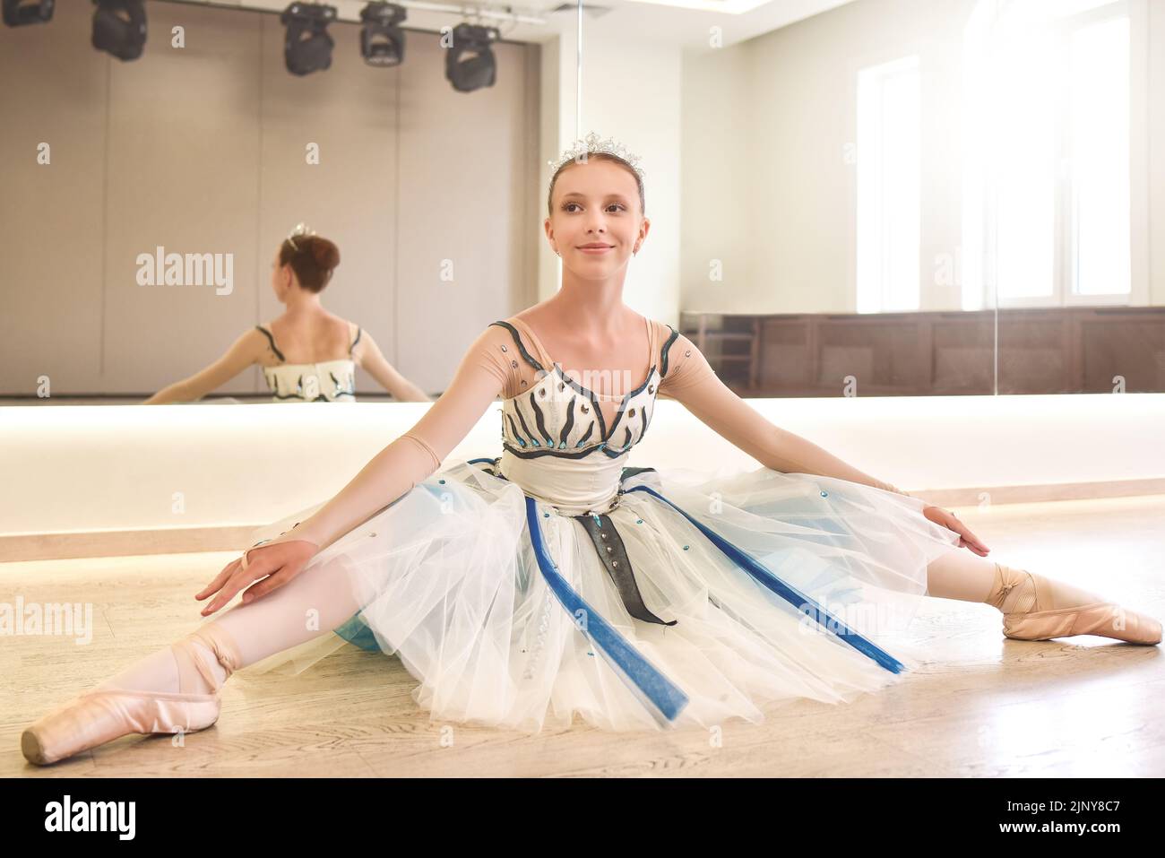 young ballerina practicing ballet poses sitting against the mirror in ...