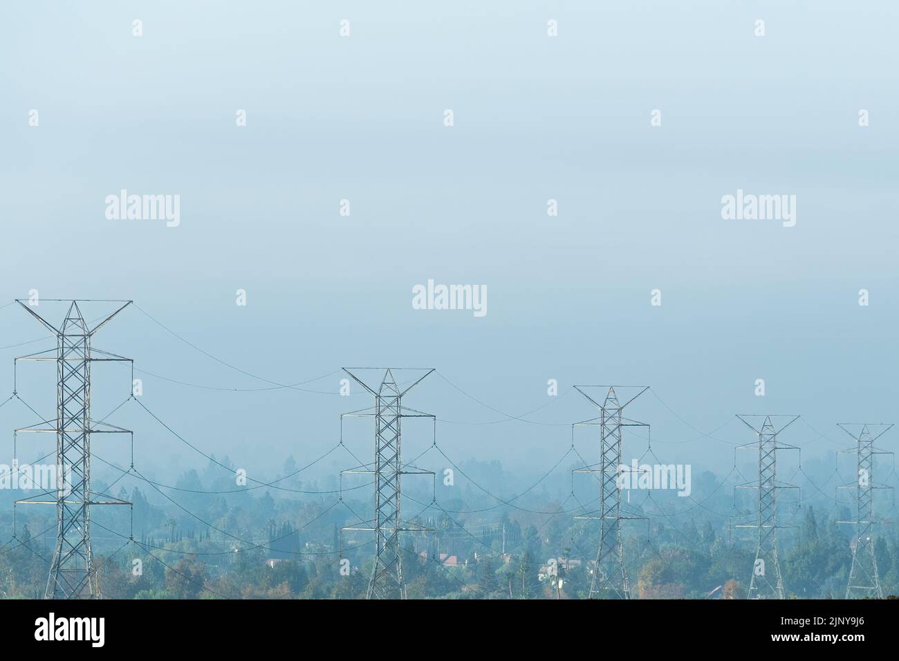 High-voltage power line towers across foggy suburban valley Stock Photo ...