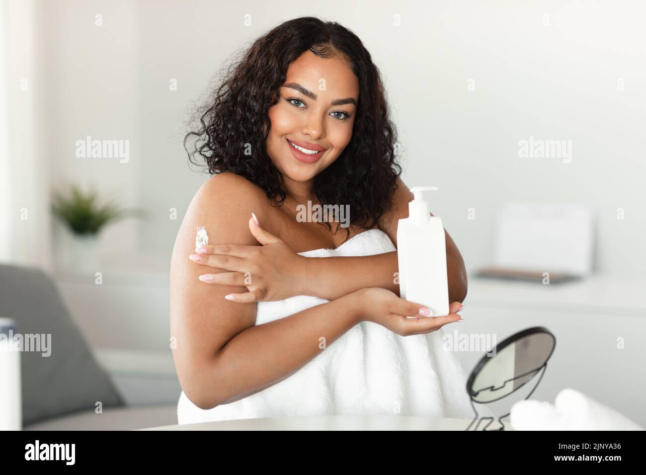 Young black chubby lady applying moisturizing body lotion on shoulder ...