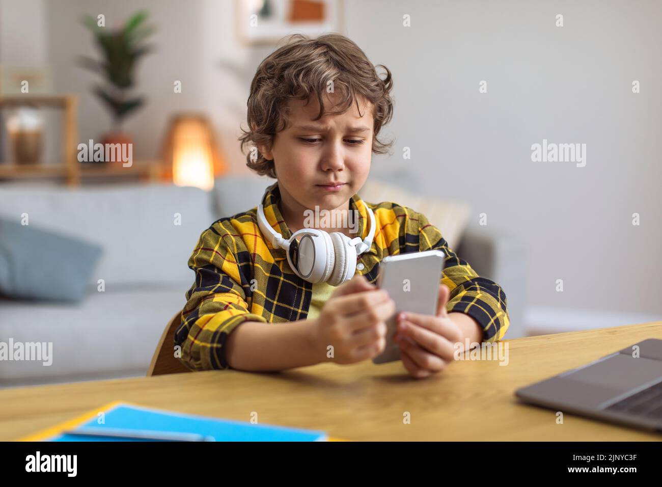 Little displeased boy looking sadly at smartphone, losing video game or ...