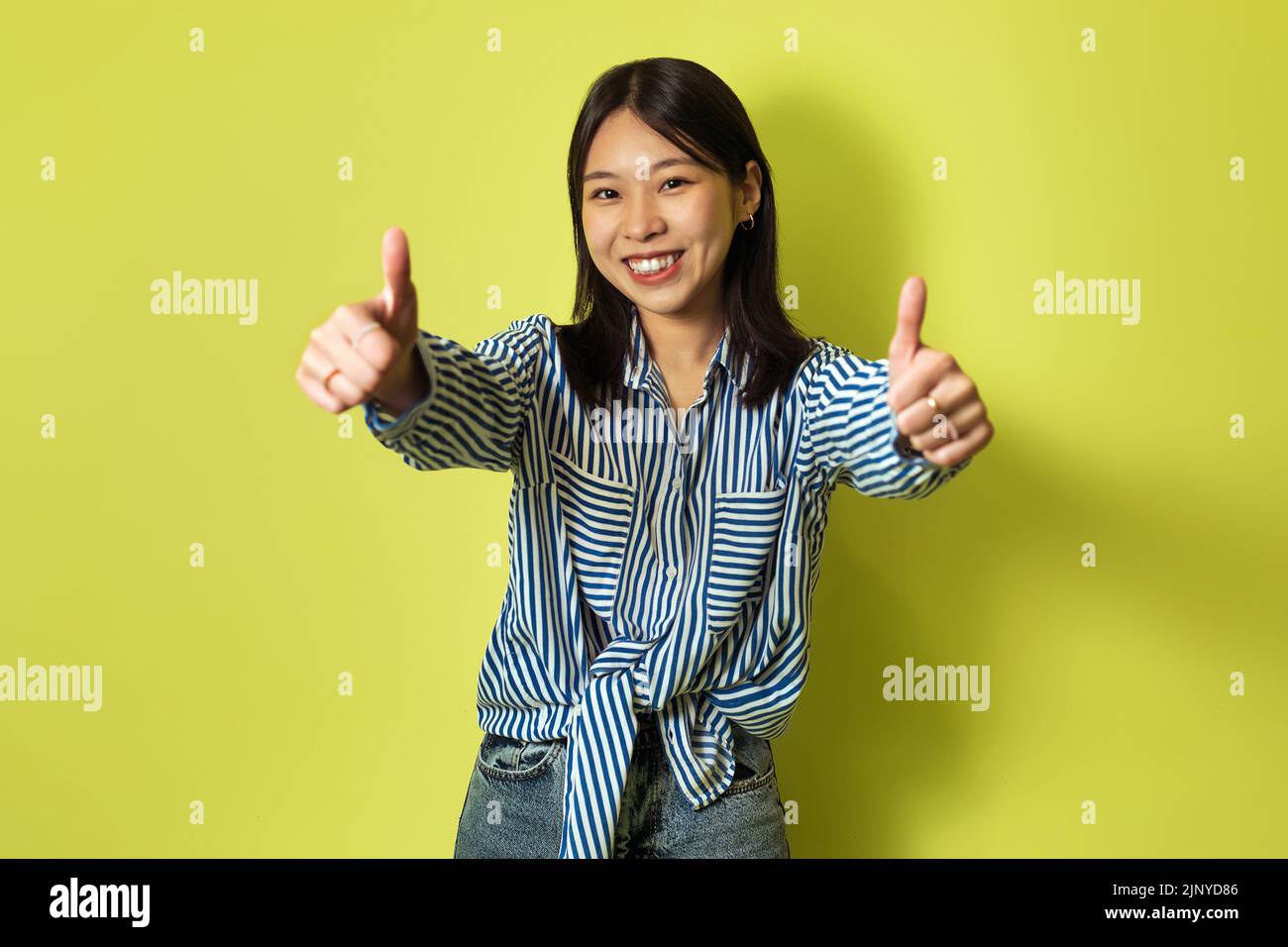 Female Gesturing Thumbs Up With Both Hands Over Yellow Background Stock ...