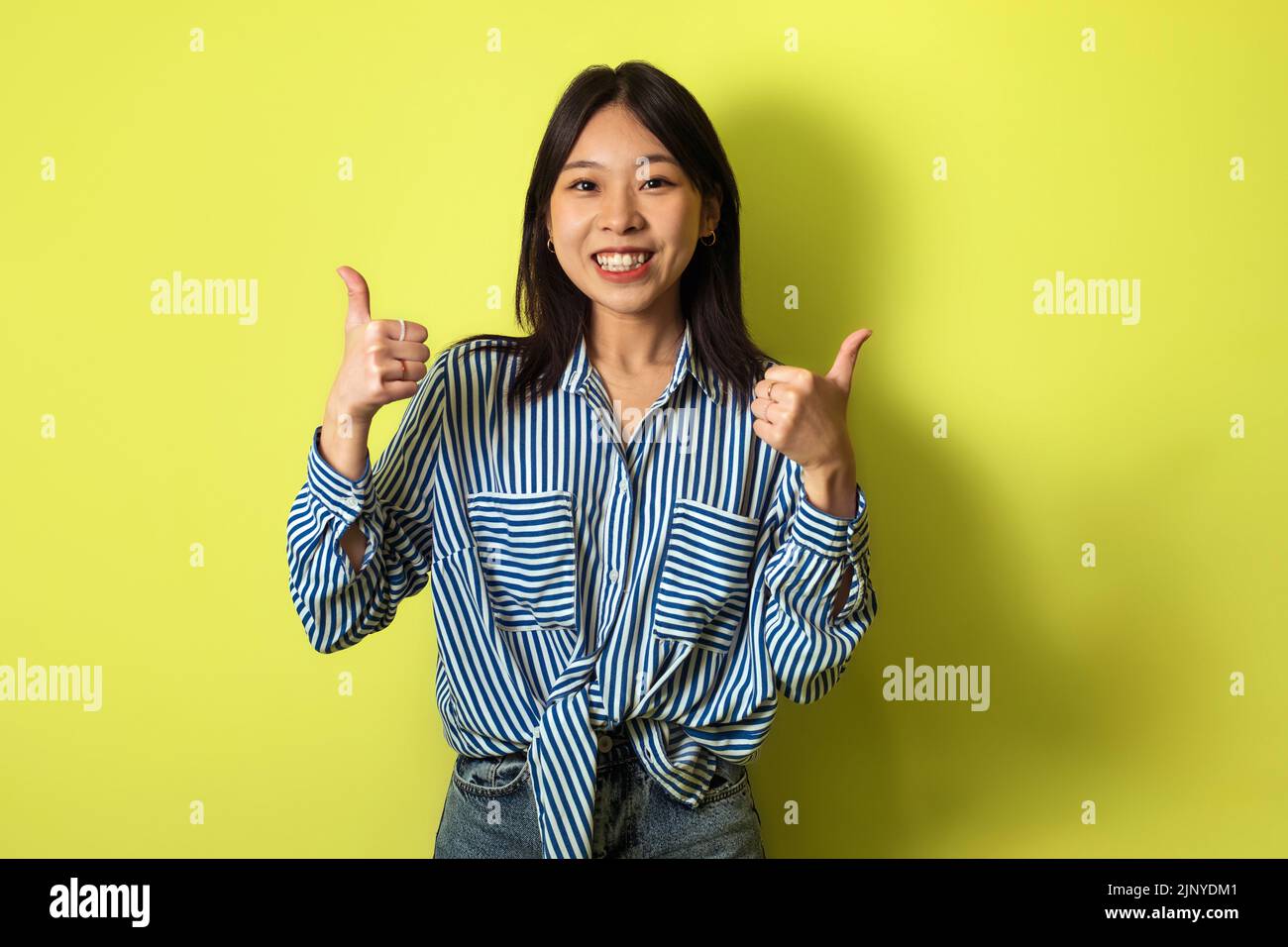 Japanese Woman Gesturing Thumbs Up With Both Hands, Yellow Background ...