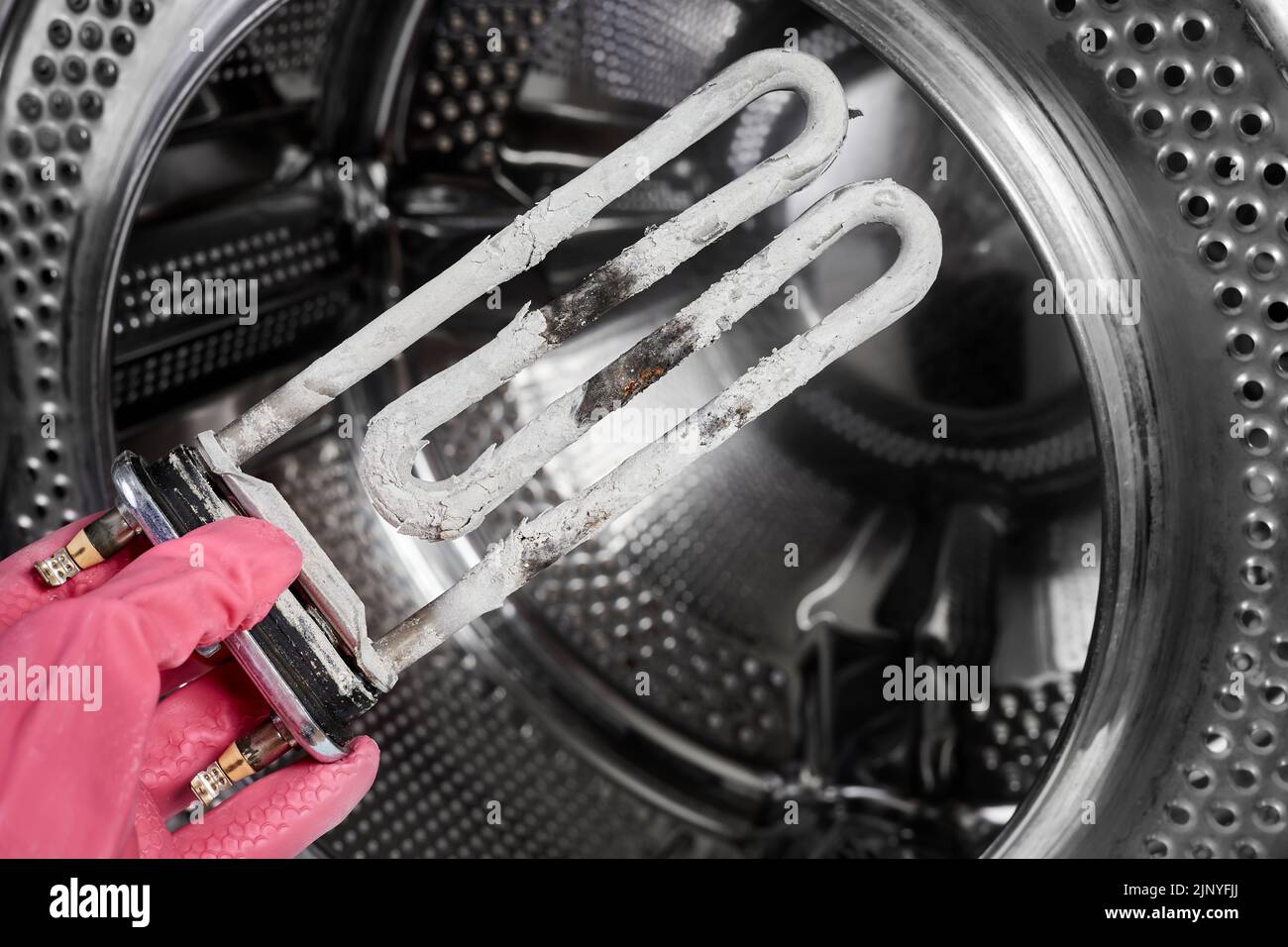 A man holds in his hand a burnt-out heating element of a washing ...
