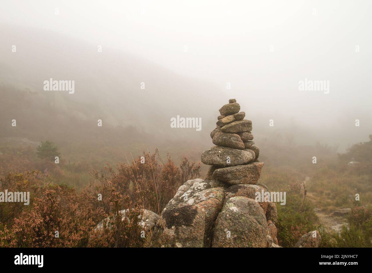 Cairn or stone marker in mountain trail with fog and bad visibility ...