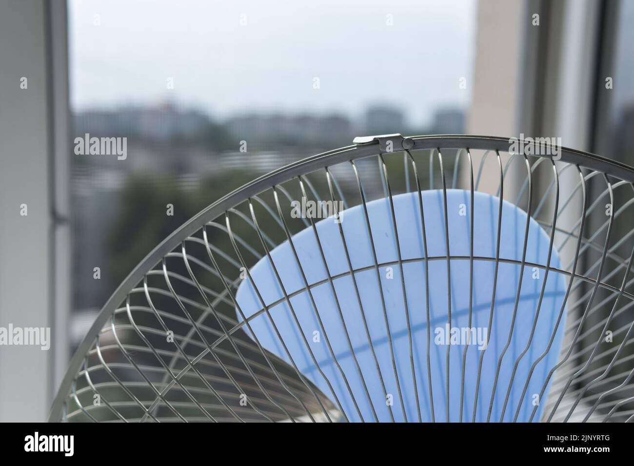 An air fan stands at a house or flat window. The background is blurred ...