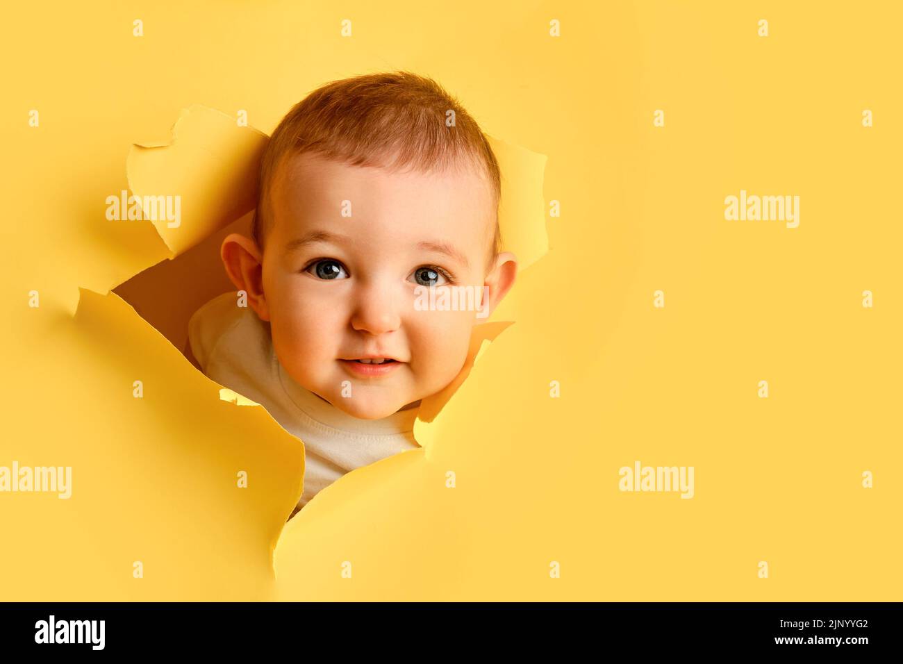 A happy child looks out of a hole in the studio yellow background ...