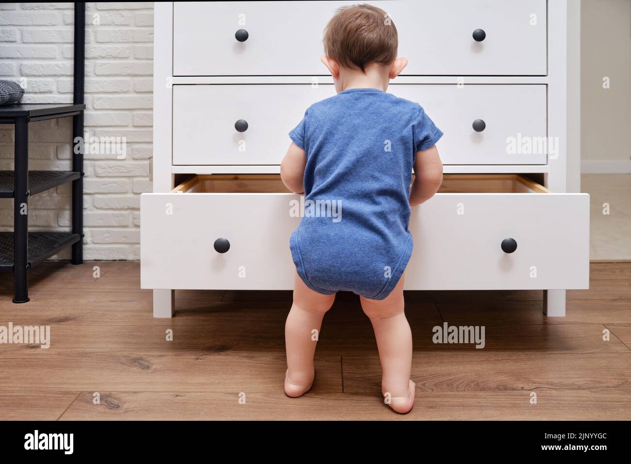 Toddler baby opens a chest of drawers. Child boy reaches into an open ...