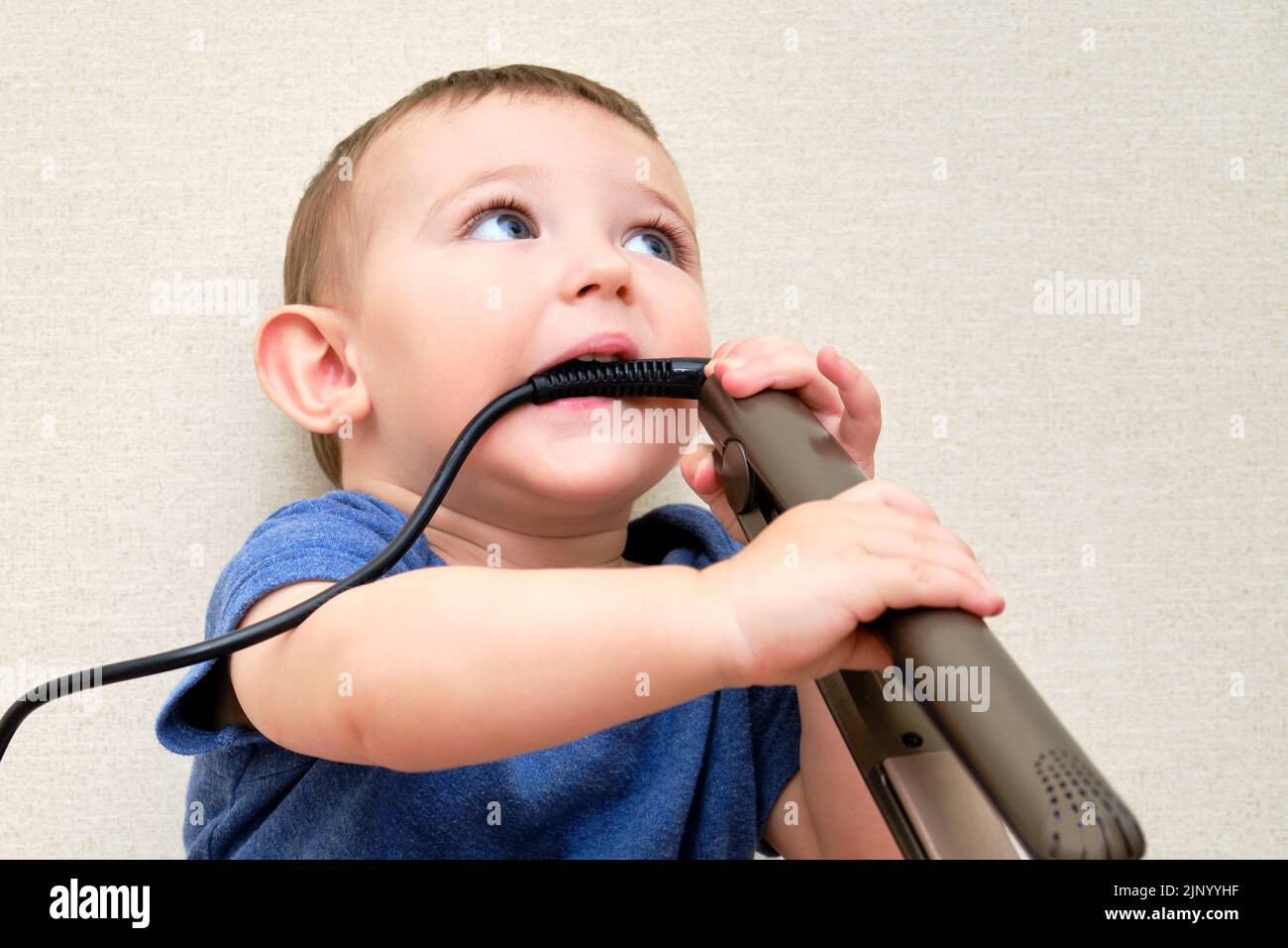 Child boy chewing on the electric wire of a curling iron. Toddler baby ...