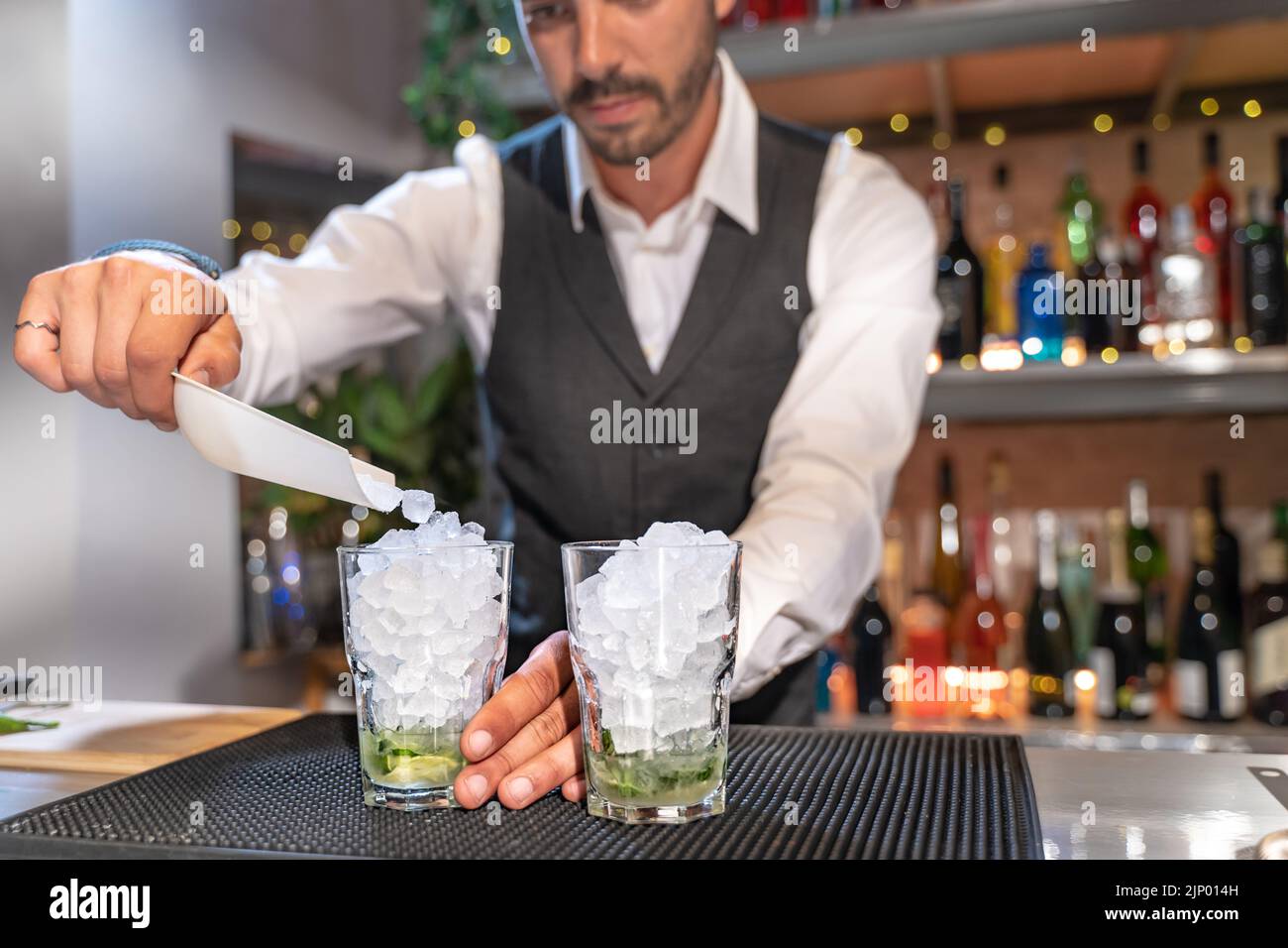 Elegant barman making cocktail Mojito in night club adding ingredients ...