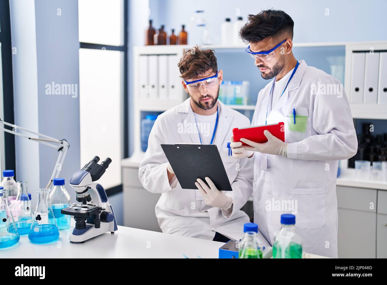 Young couple wearing scientist uniform using touchpad at laboratory ...